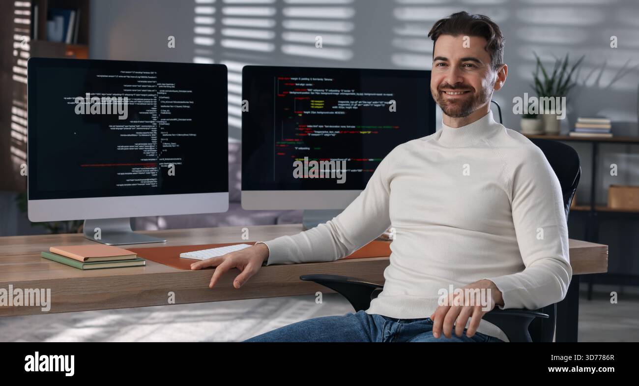 Smiling programmer on chair near table at workplace Stock Photo - Alamy