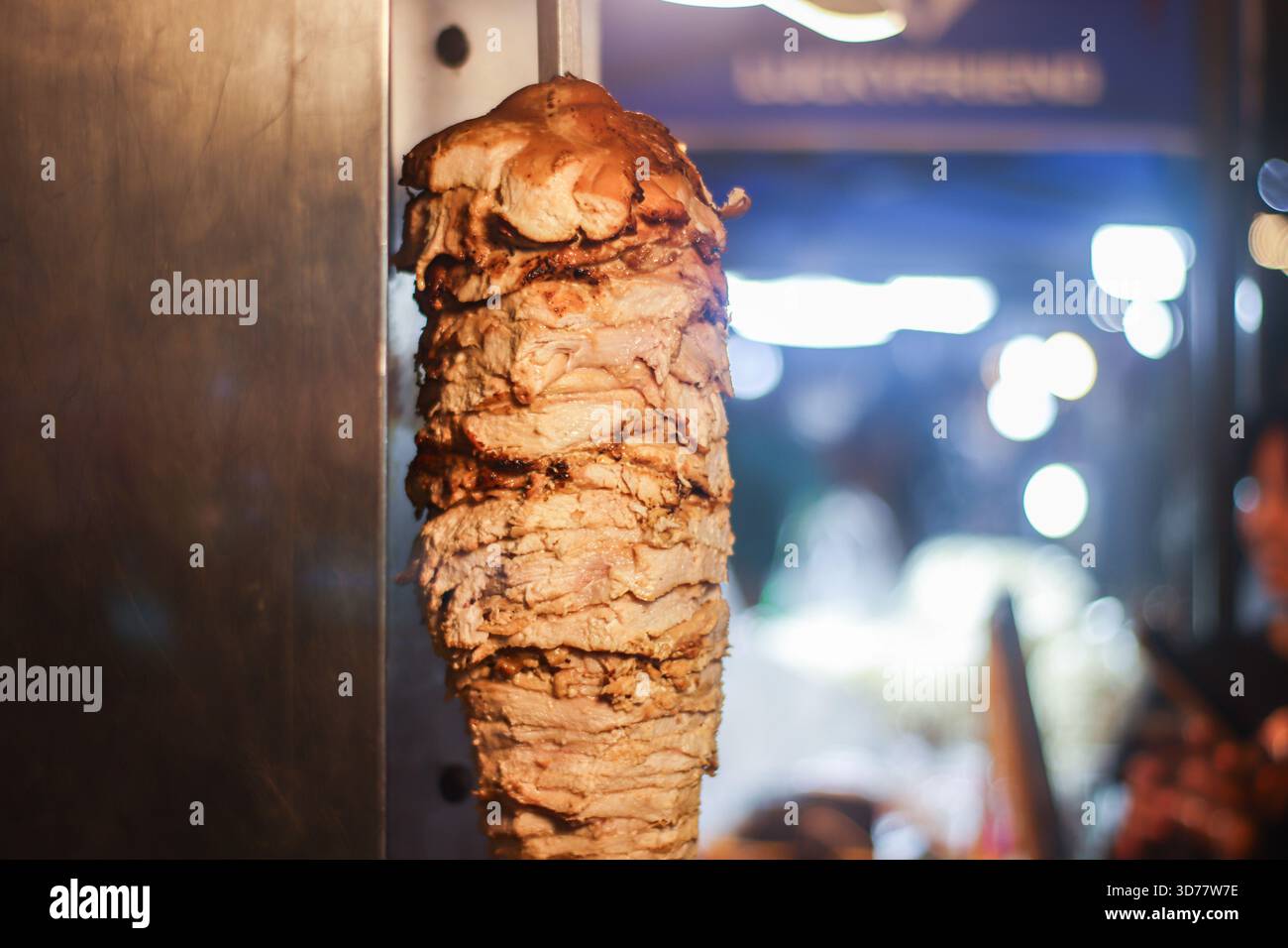 Vertical rotisserie kebab meat with night market bokeh, highlighting ...