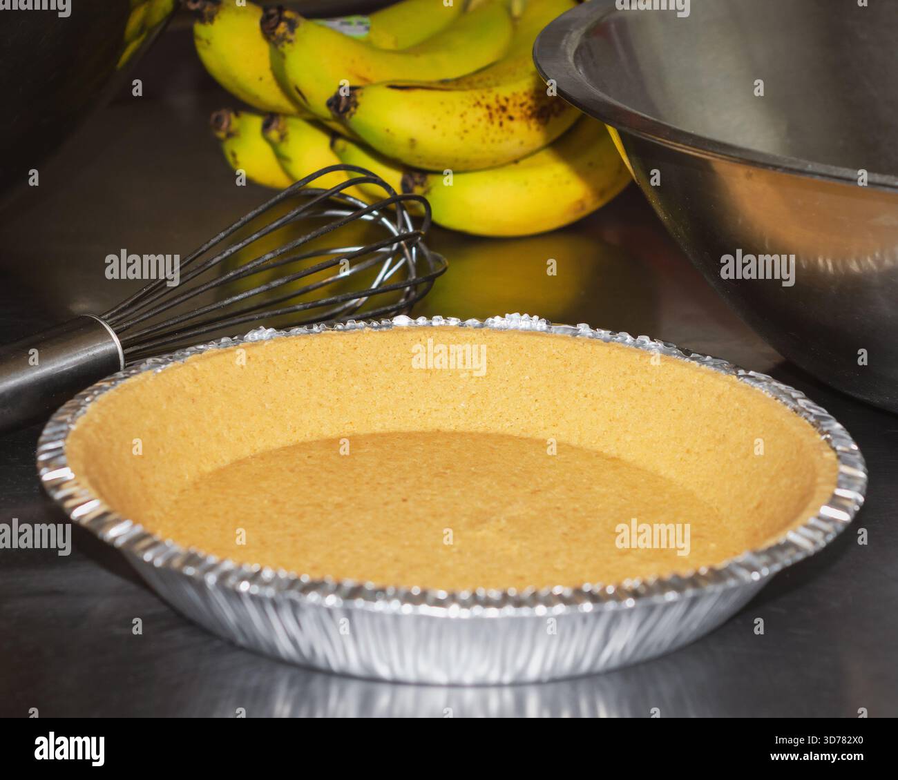 A ready-made graham cracker pie crust on a stainless steel counter next ...