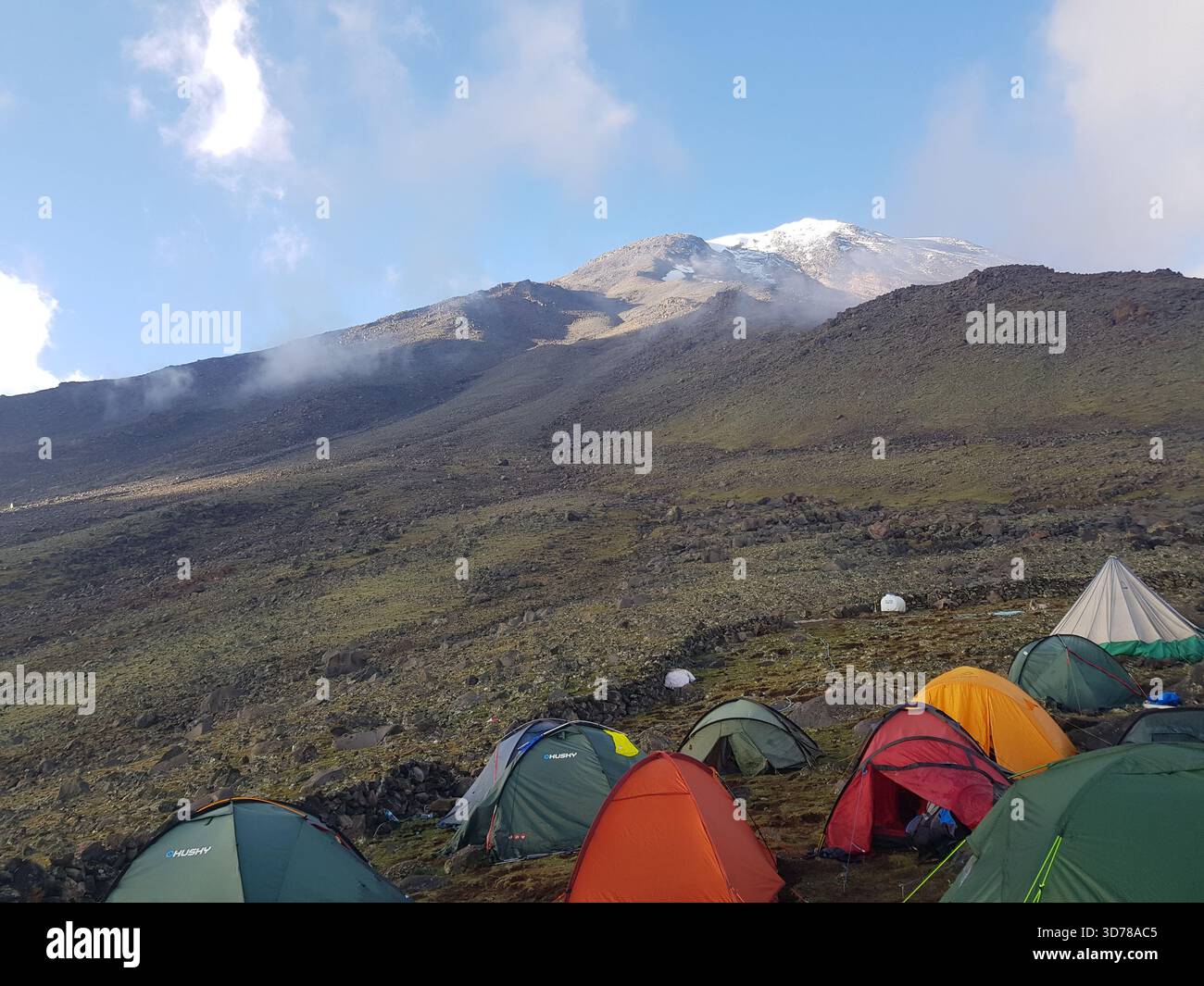 High-altitude mountain camp set beneath a rugged volcanic slope, with ...