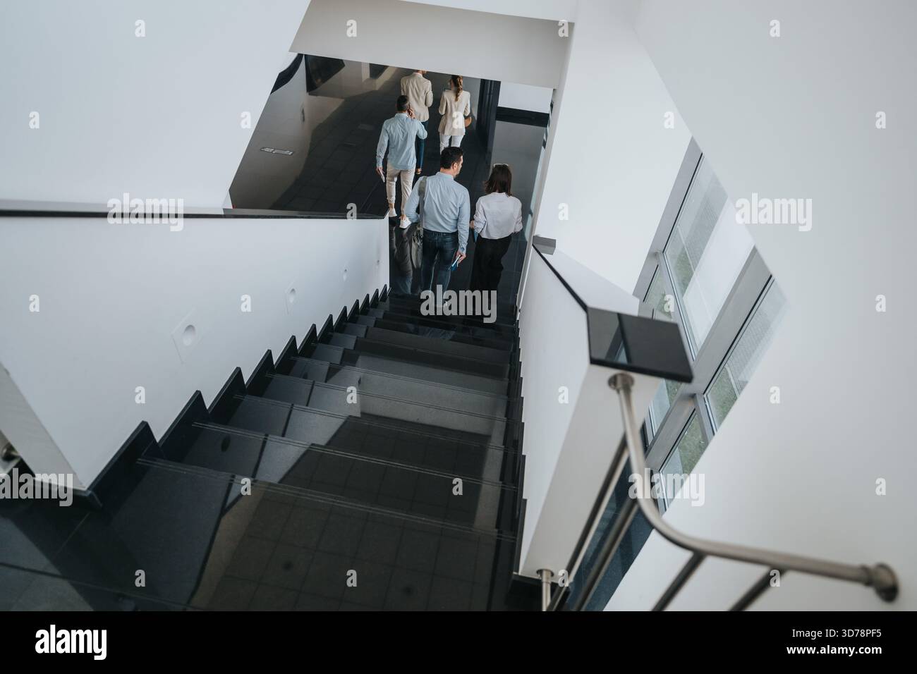 People descend a modern office staircase in a bright, minimalist ...