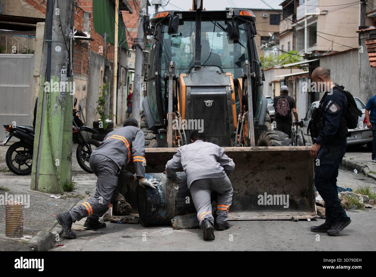 Workers push a barrel filled with concrete into a bulldozer during a ...