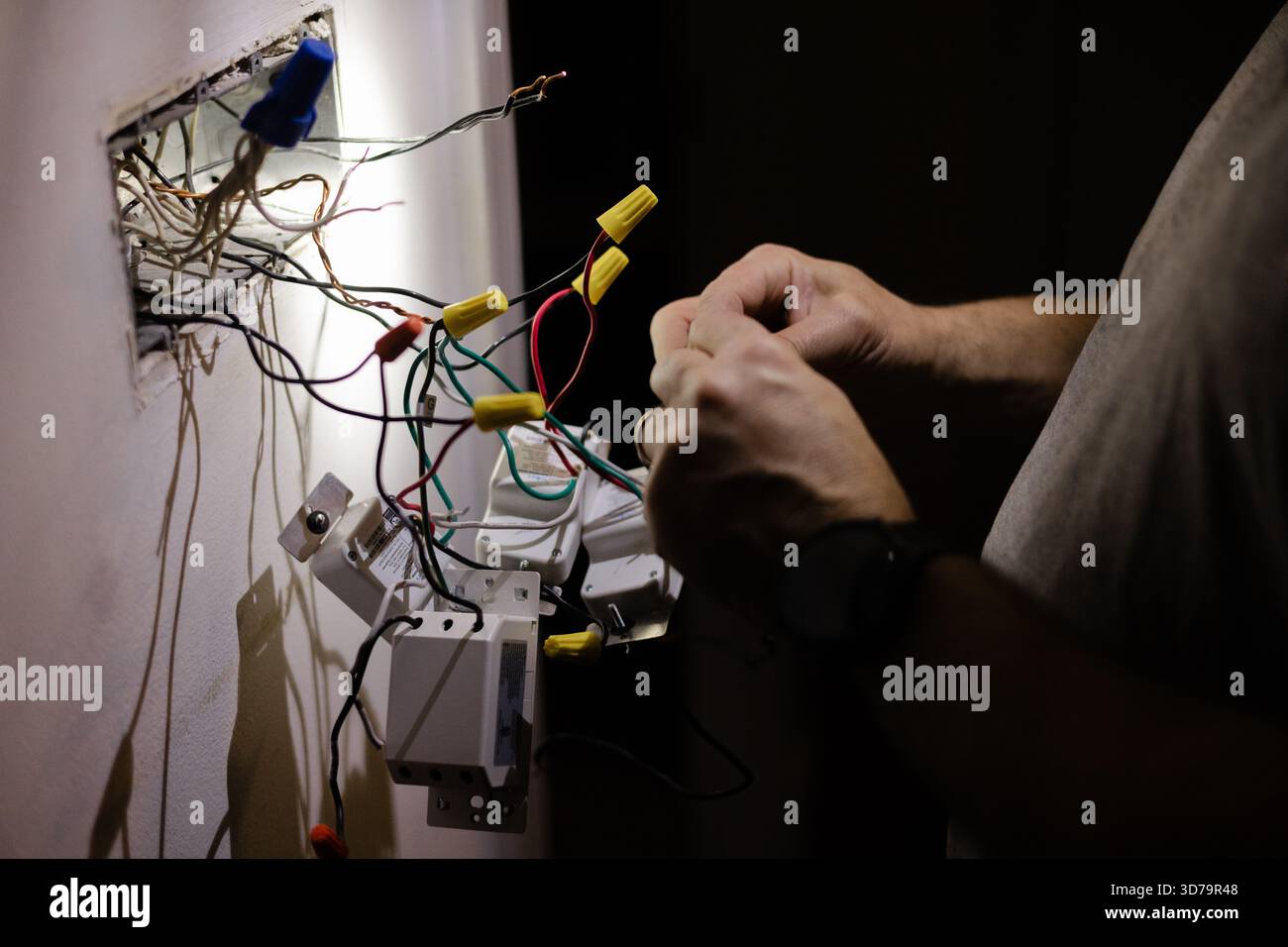 A person connects colorful electrical wires in a small, dark space ...