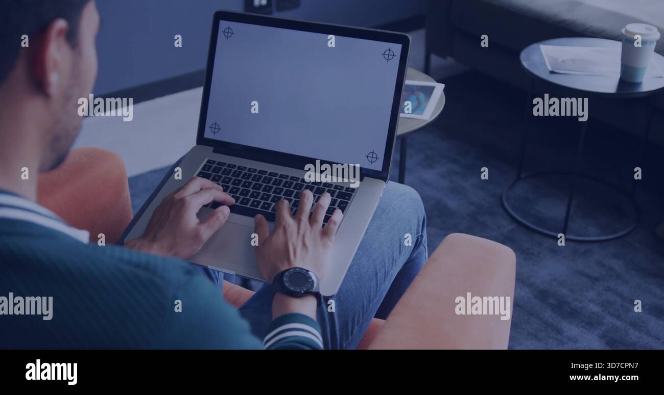 Typing man wearing green sweater on orange armchair in lounge, with ...