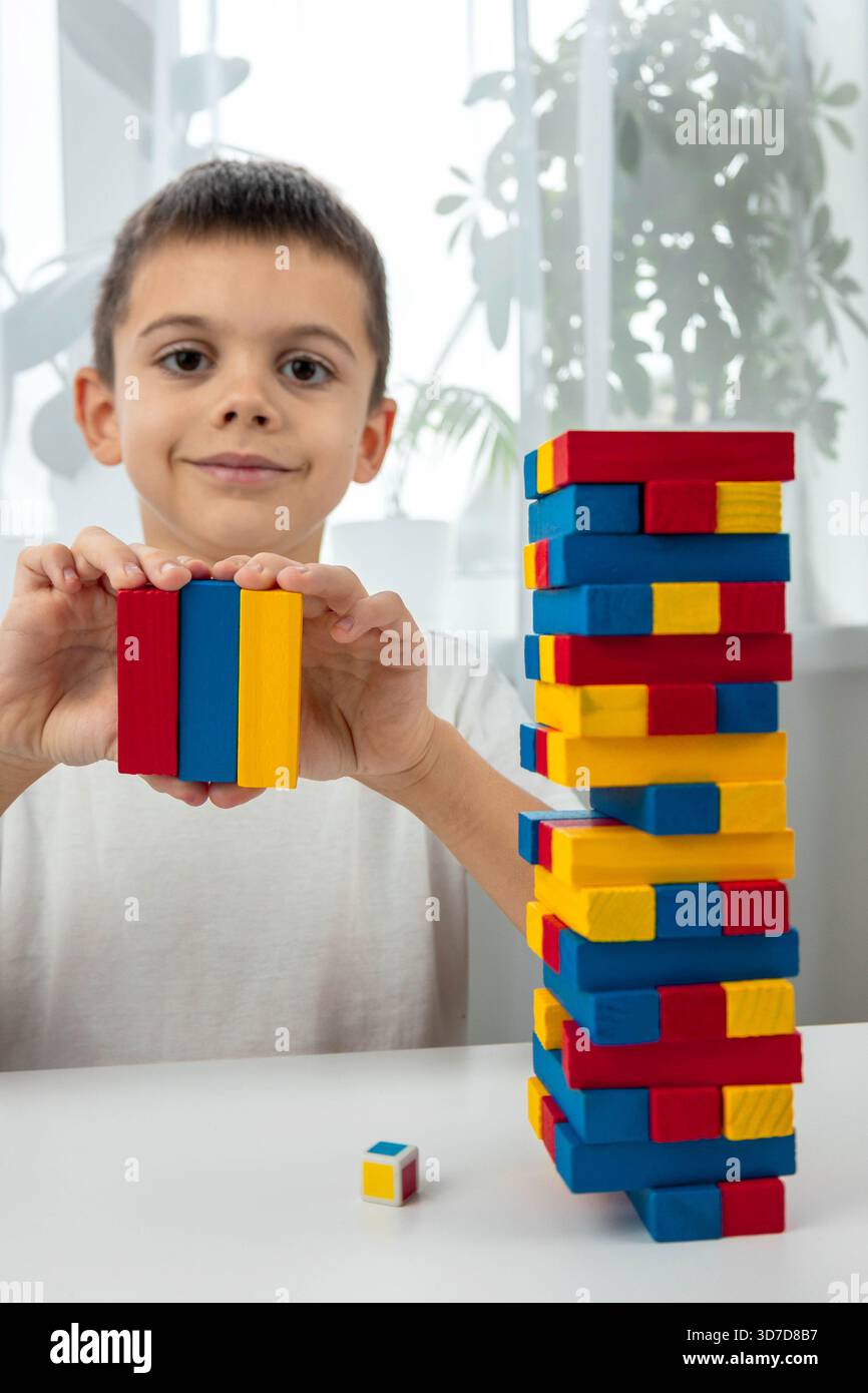 Boy playing the Jenga board game, carefully pulling a colored wooden ...
