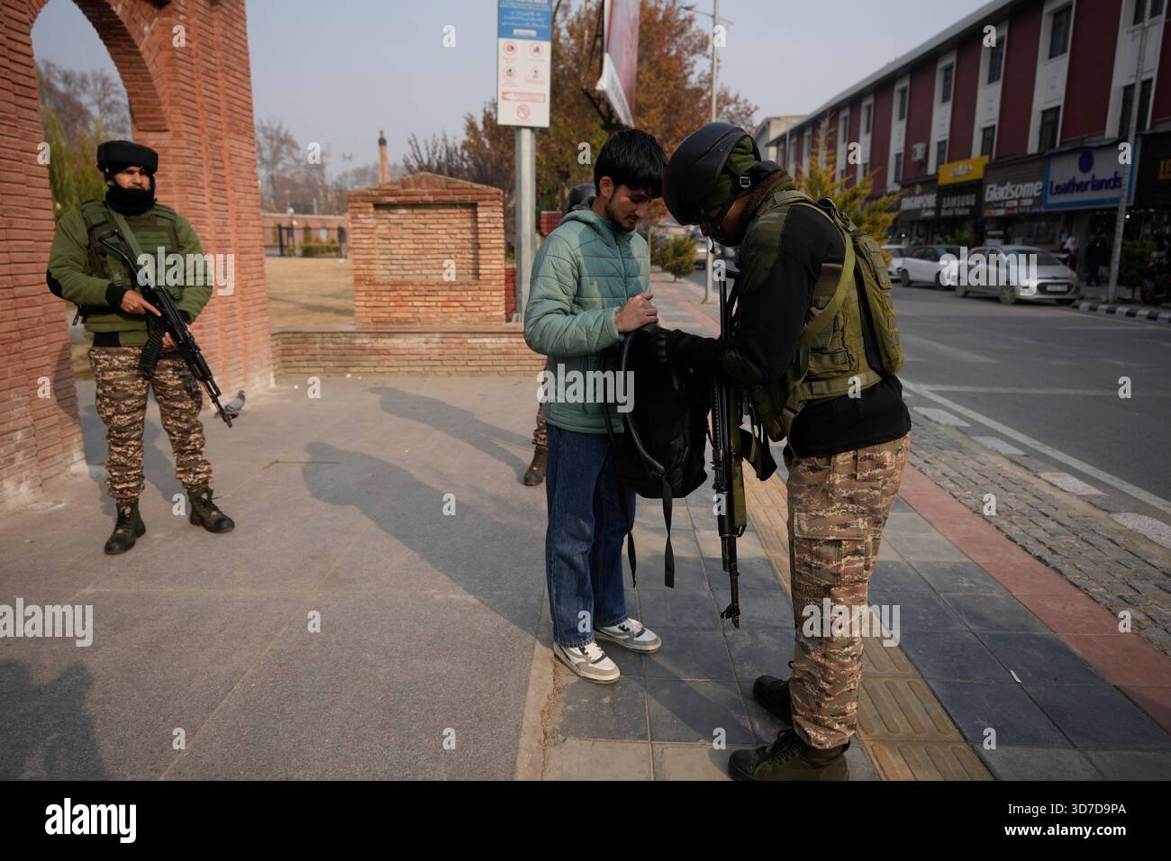 An Indian paramilitary soldier checks the bag of a young man during a ...
