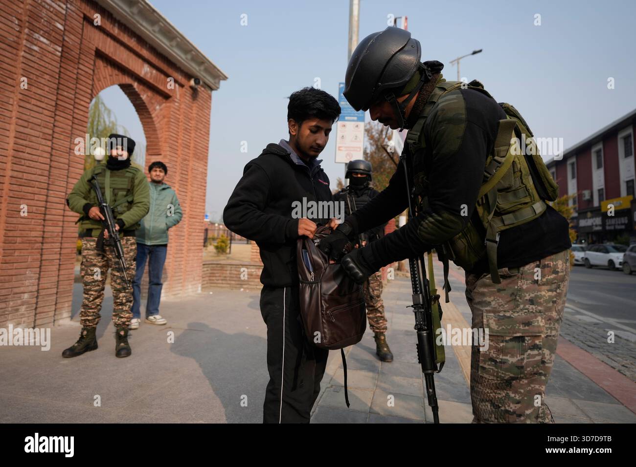 An Indian paramilitary soldier checks the bag of a young man during a ...