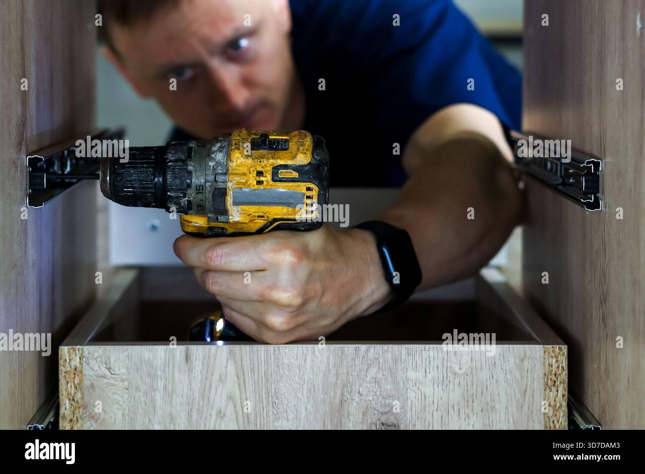 Worker screwing metal slide for drawer in wooden cabinet. Handyman ...
