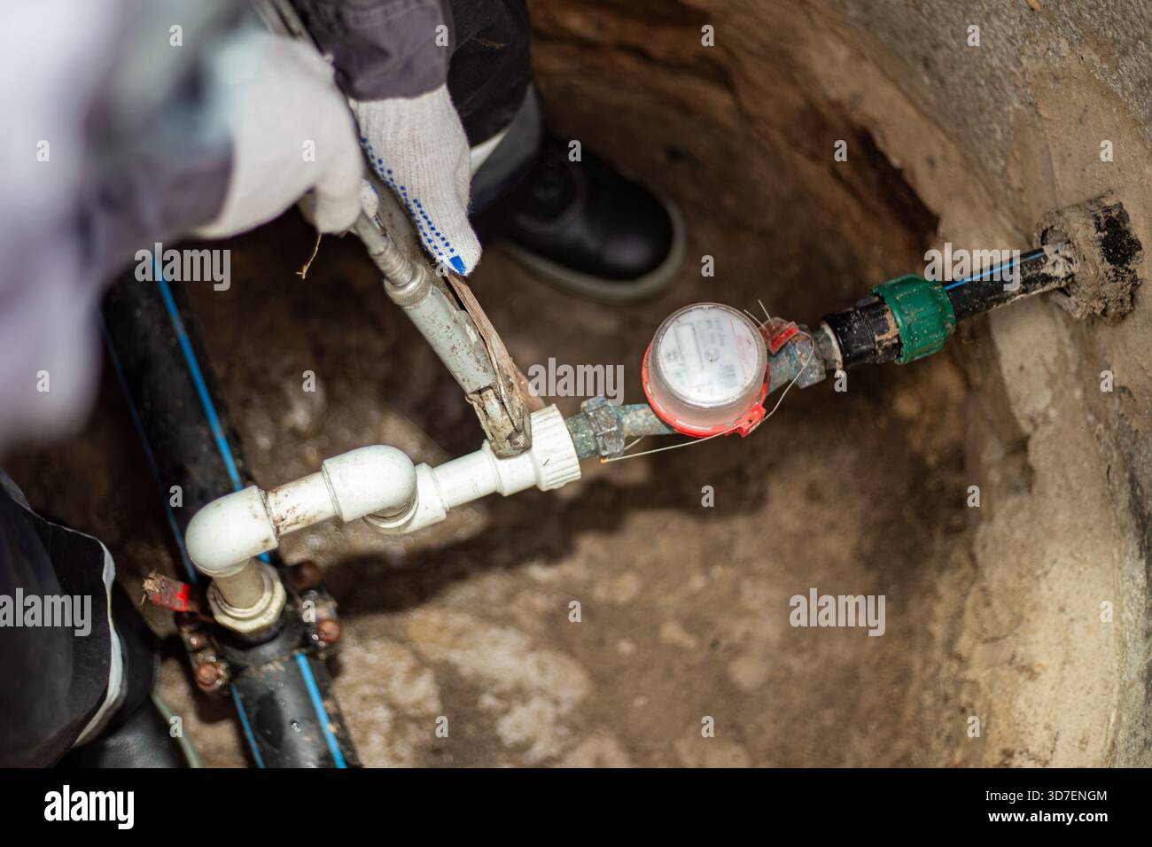 A plumber tightens a threaded fitting on a pipe in a water well with an ...