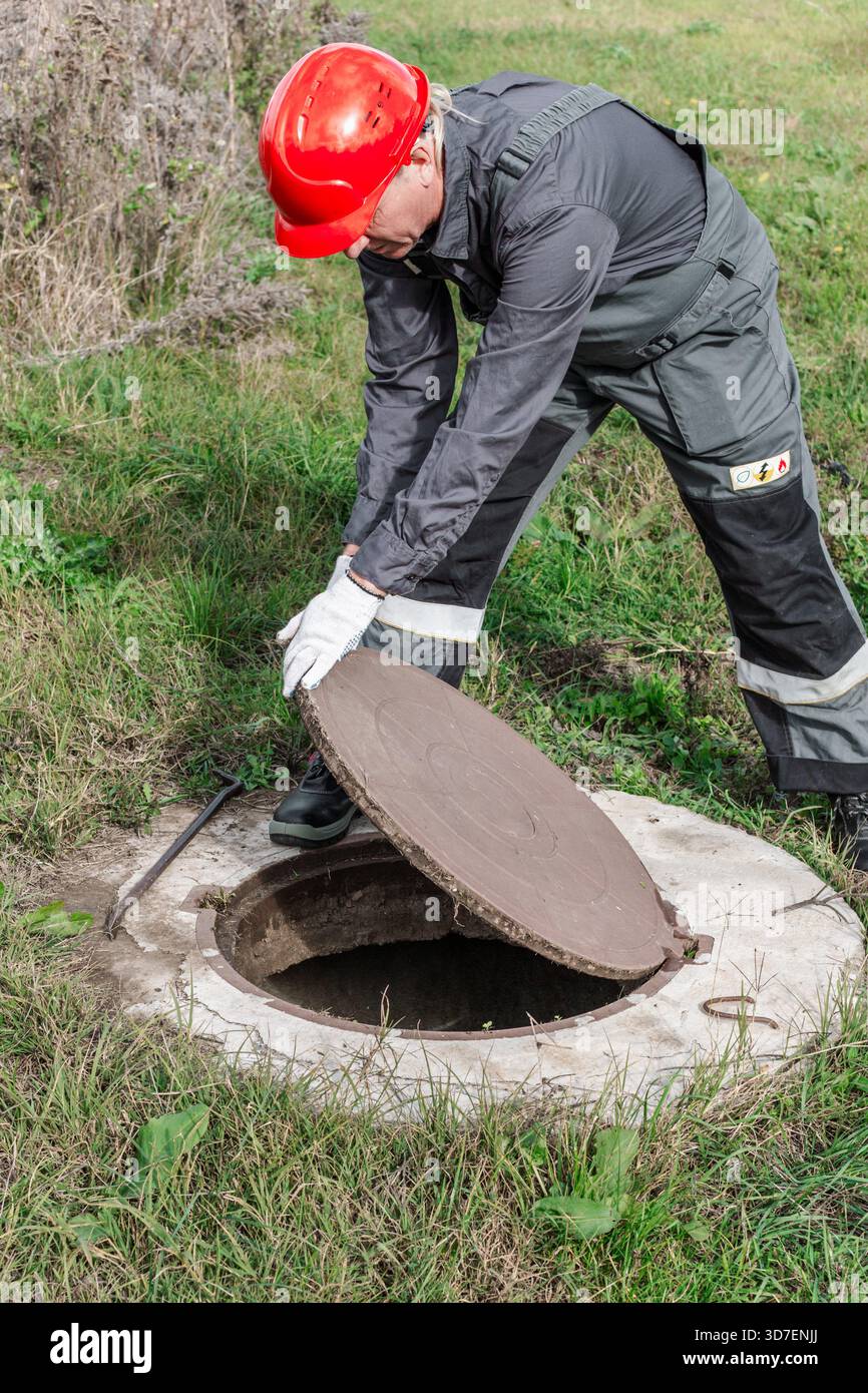 A male utility worker opens the manhole cover of a water well to check ...
