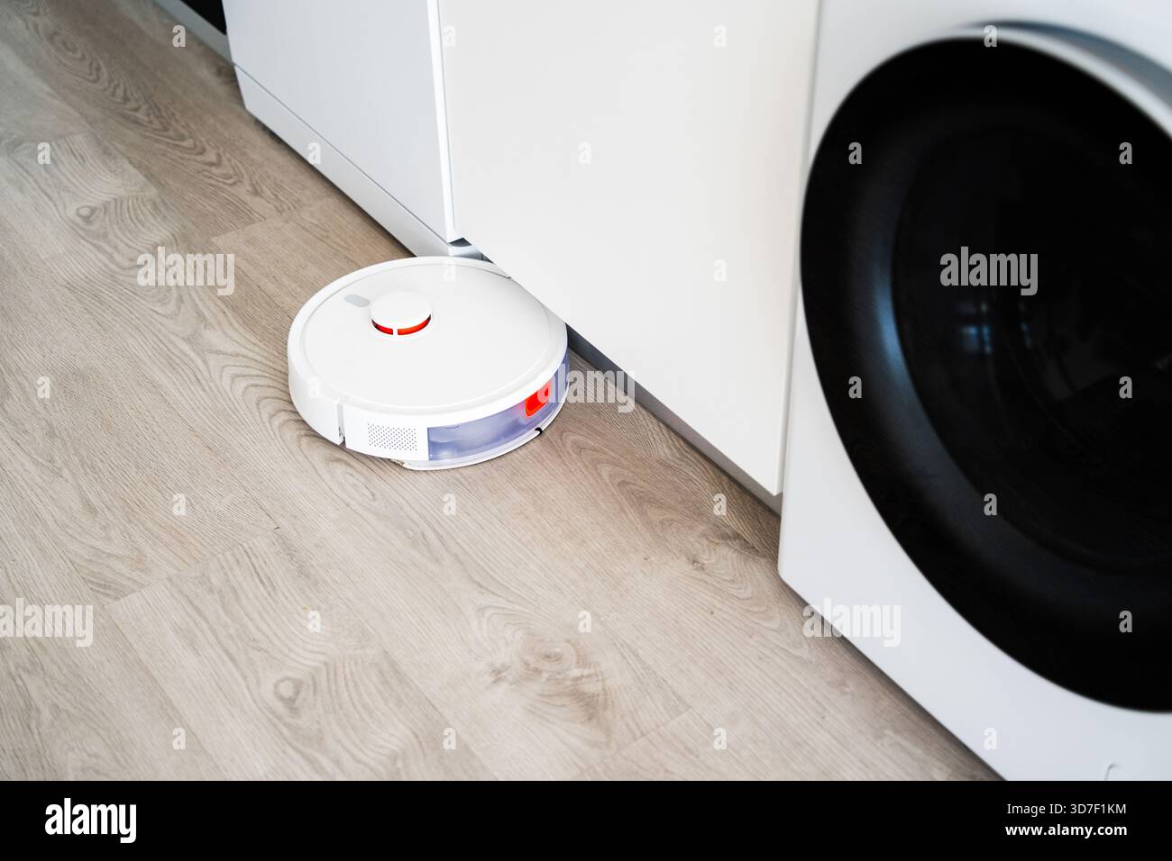 Robot vacuum cleaner moving near washing machine on wooden floor inside ...