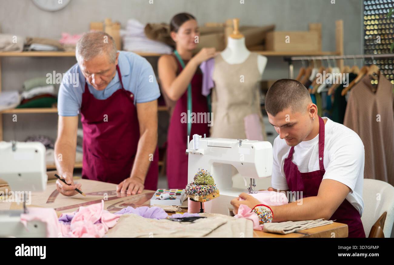 young tailor sews next to a mature worker and a female tailor Stock ...