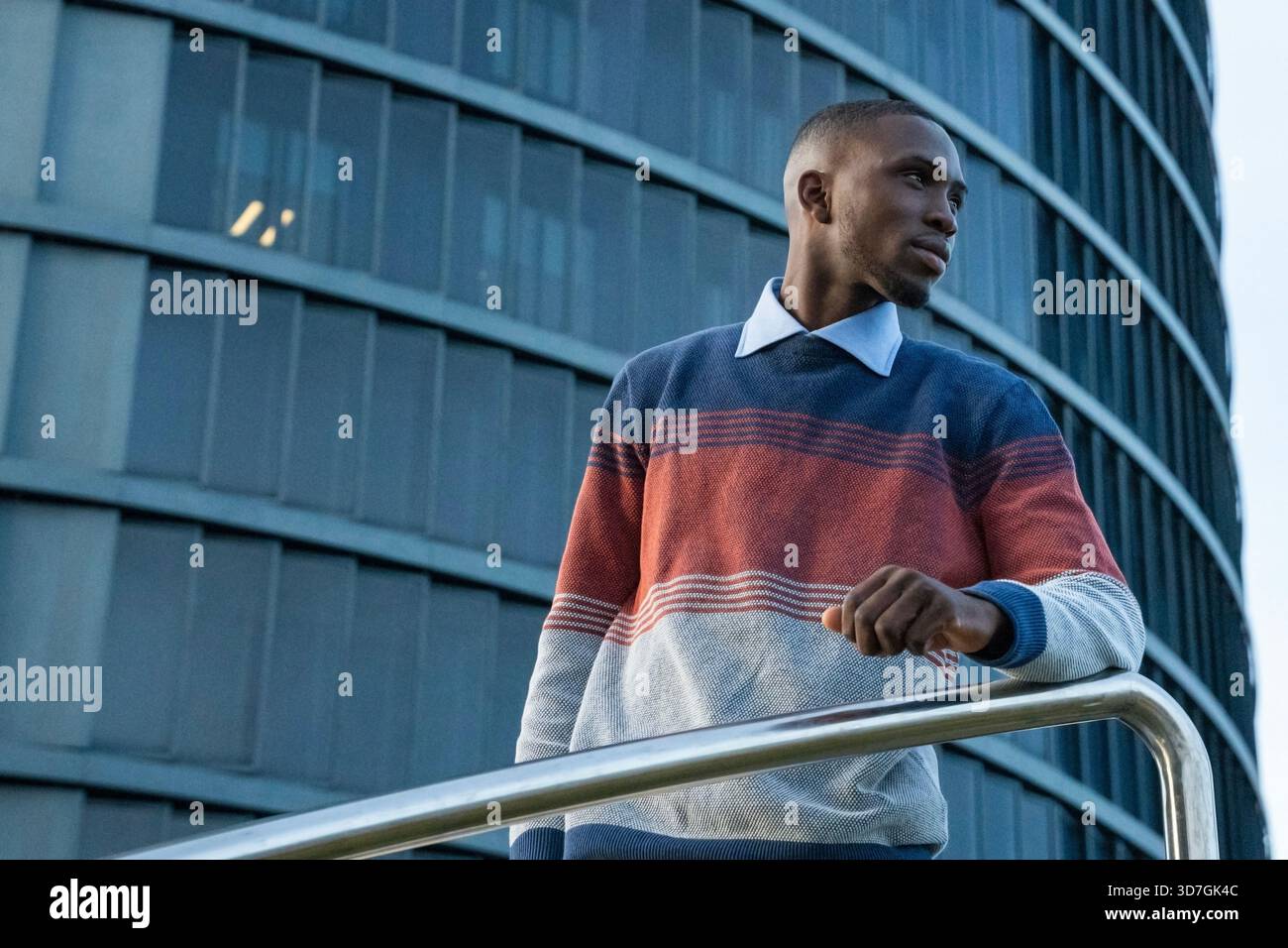 A young man stands confidently on a balcony railing, wearing a colorful ...