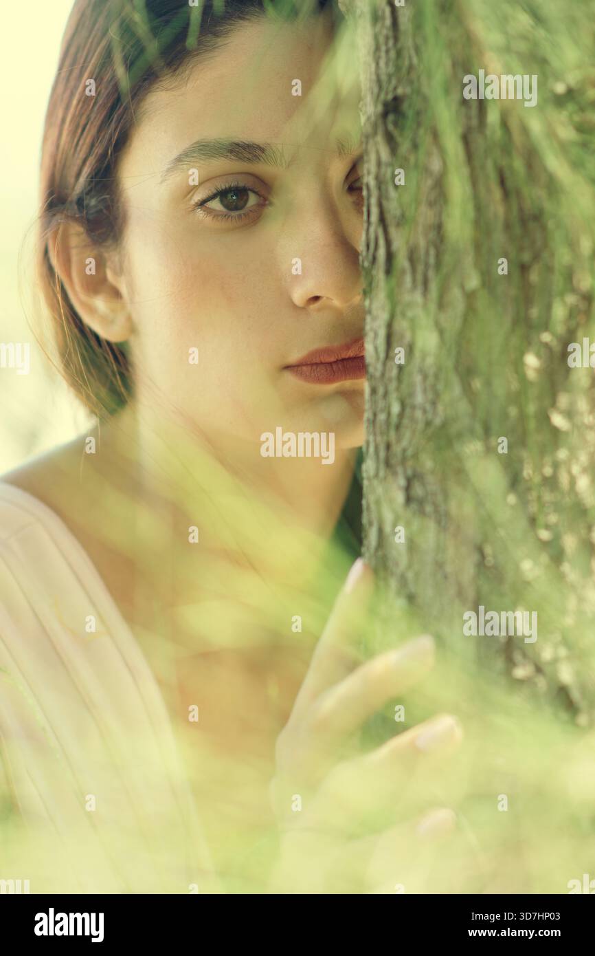 Scared woman hiding behind tree Stock Photo - Alamy