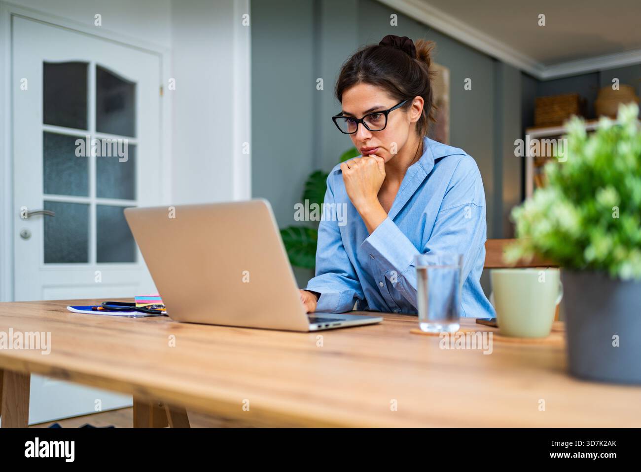 Focused female professional in glasses working on a laptop PC, chin ...