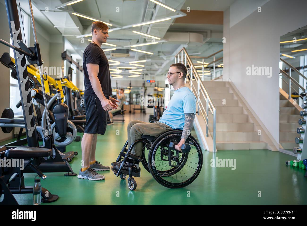 Personal trainer assists disabled man in wheelchair in gym ...