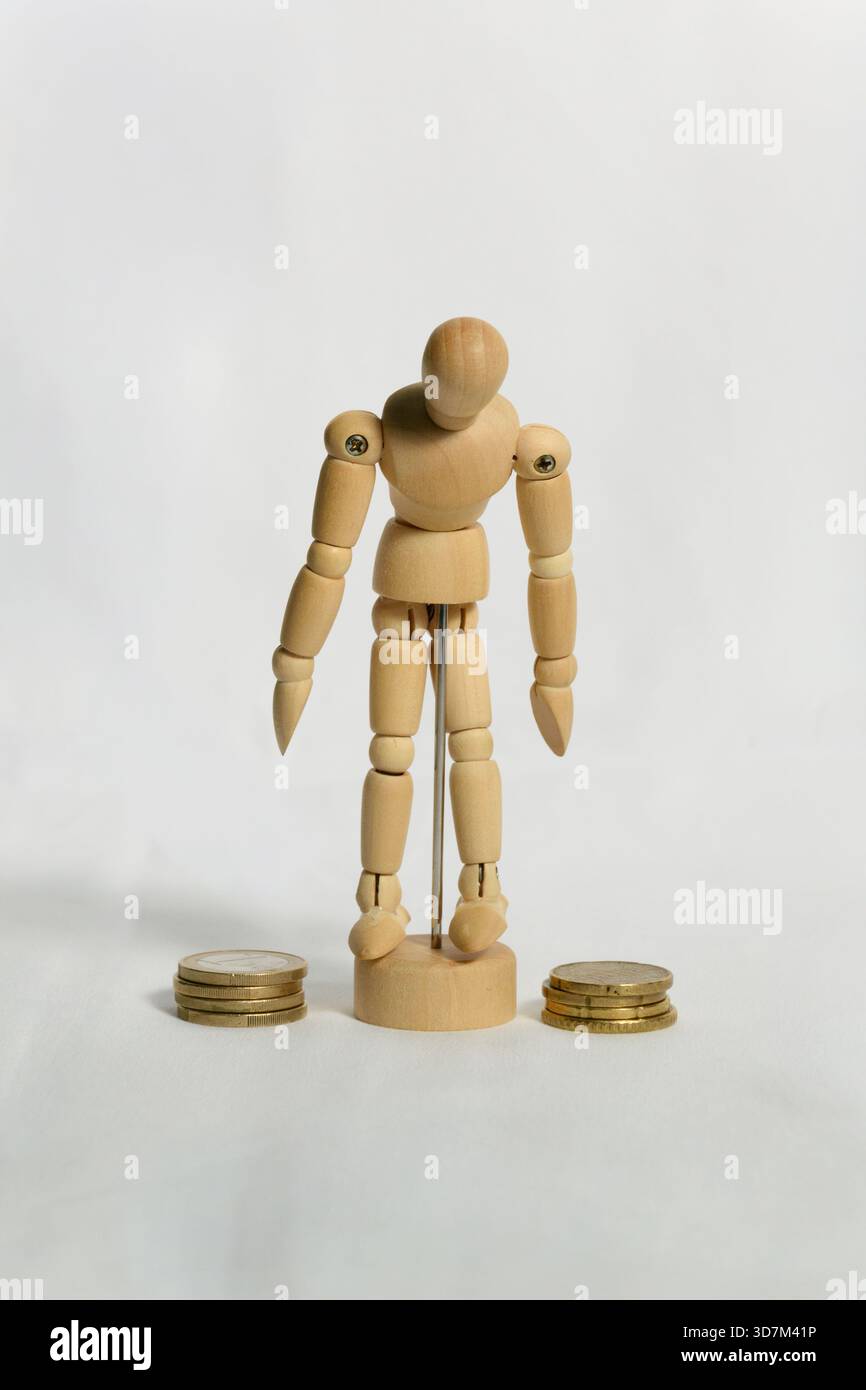 Wooden mannequin standing sadly between two piles of coins on a white ...