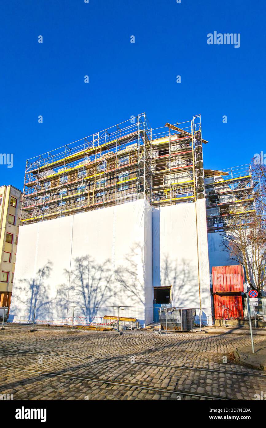 A multi-story building wrapped in protective sheeting and surrounded by ...