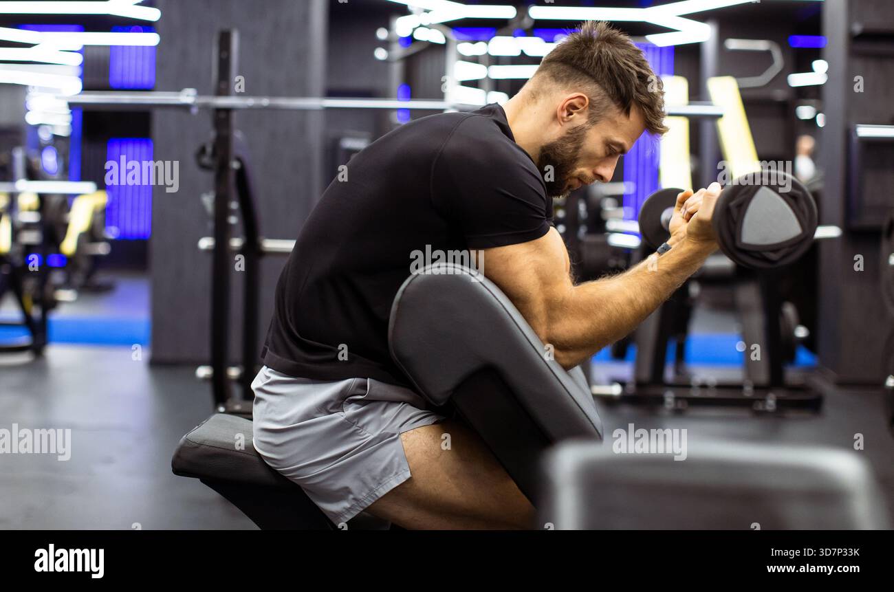A man is engaged in bicep curls at a well-equipped gym. He focuses on ...
