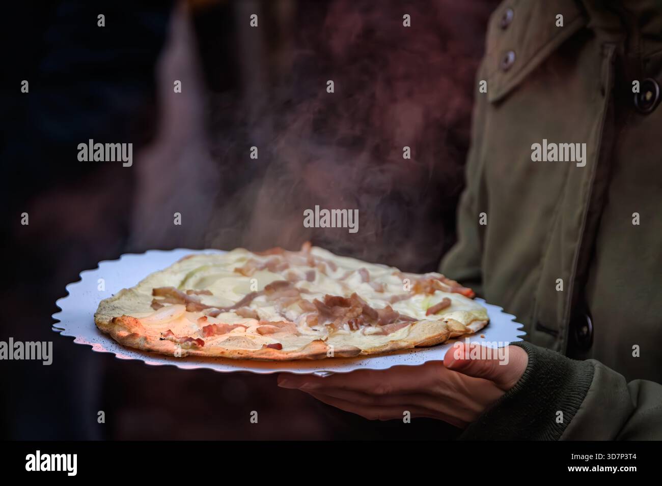A person holds a steaming hot traditional Alsatian tarte flambee ...