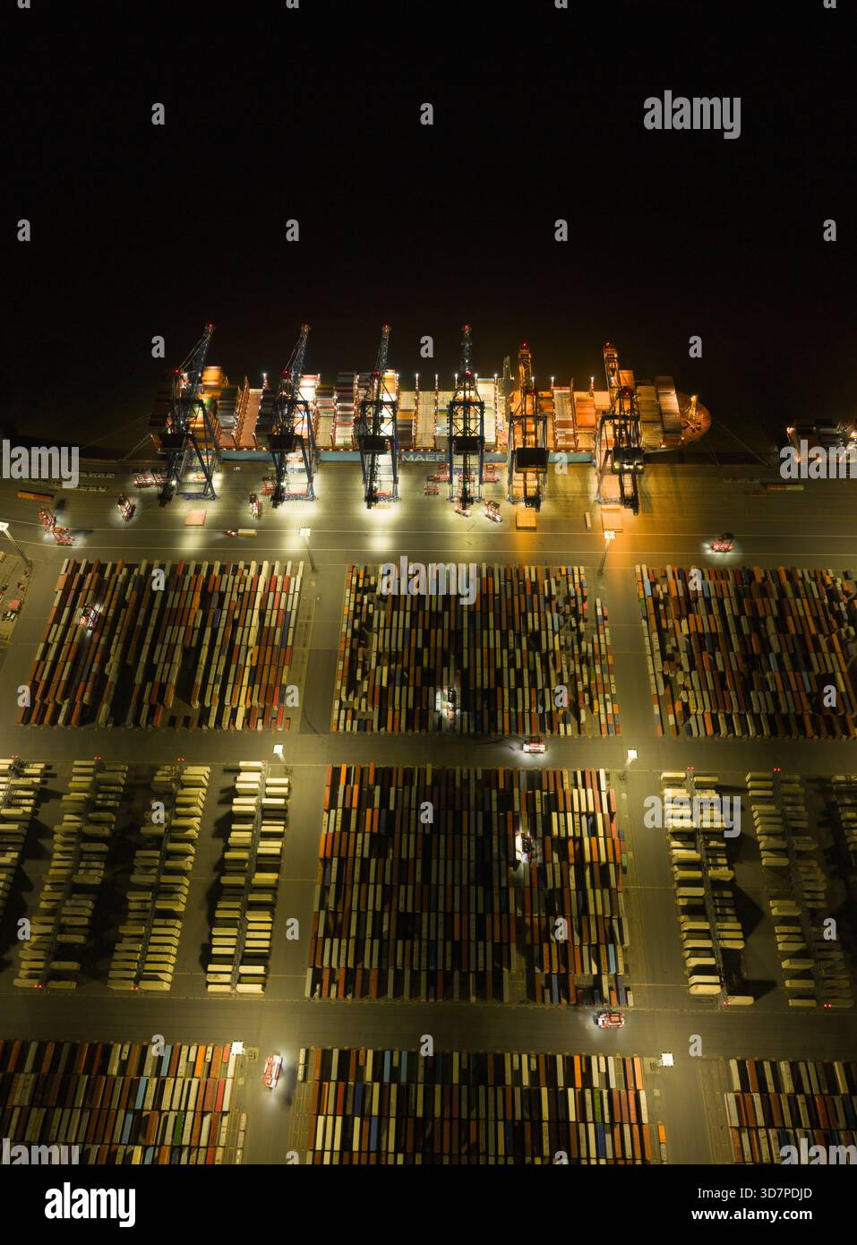 Aerial view of brightly lit shipping containers and cranes create ...