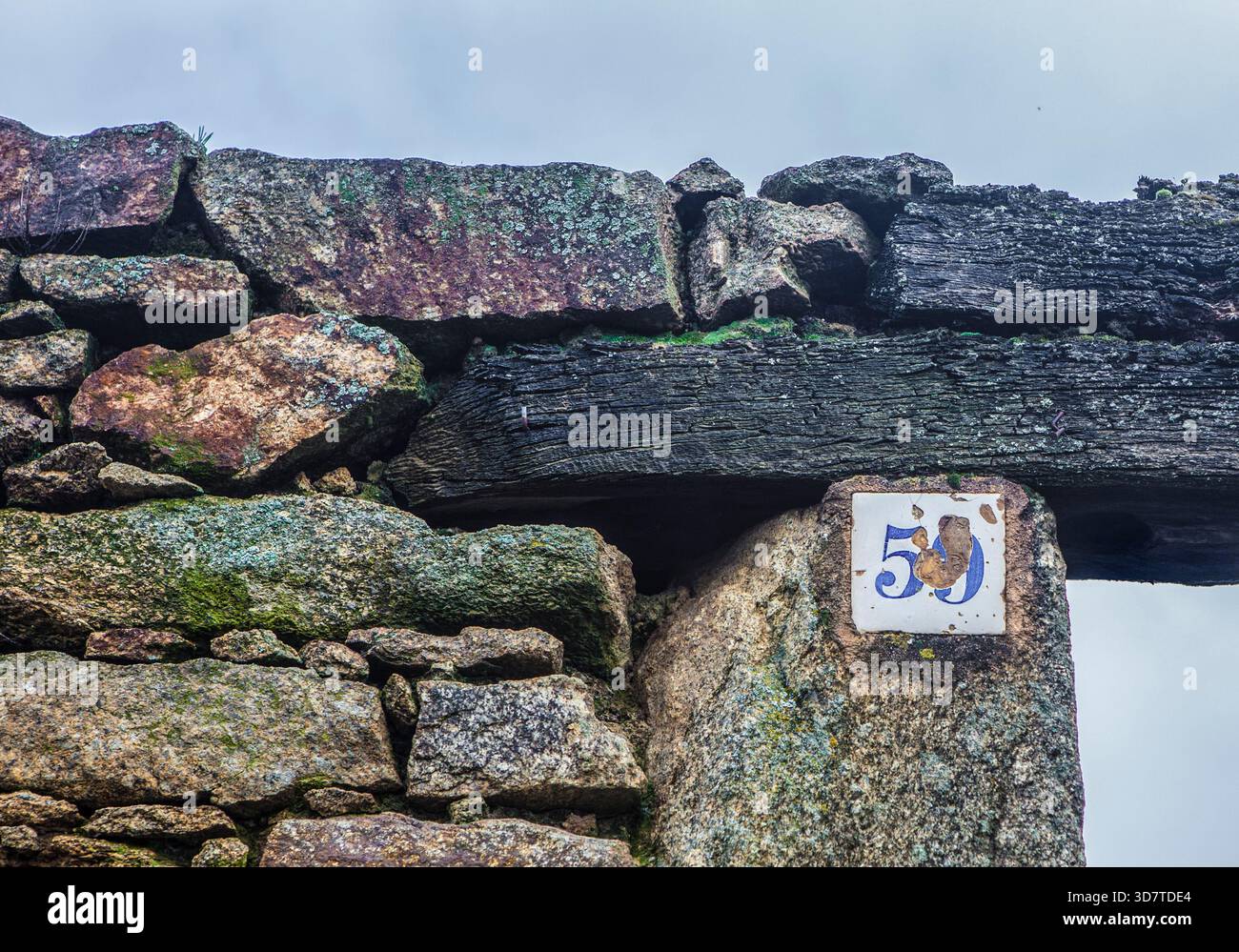 Rustic house number 59 placed on the wooden lintel of a ruined stone ...