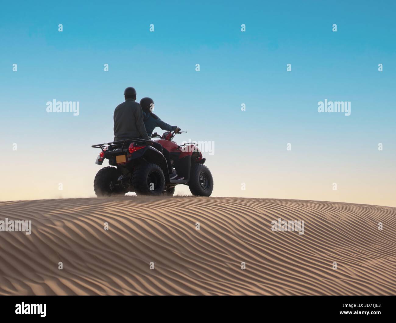 Two men on quad bike riding on sand dunes in desert during golden time ...