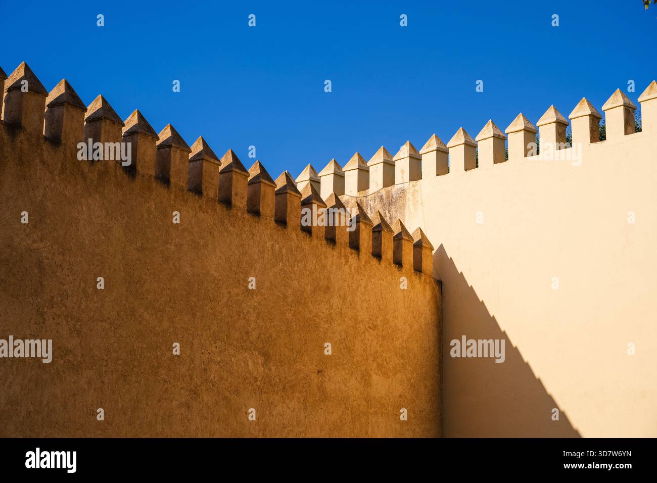 Sunlit stone walls with triangular crenellations against a clear blue ...