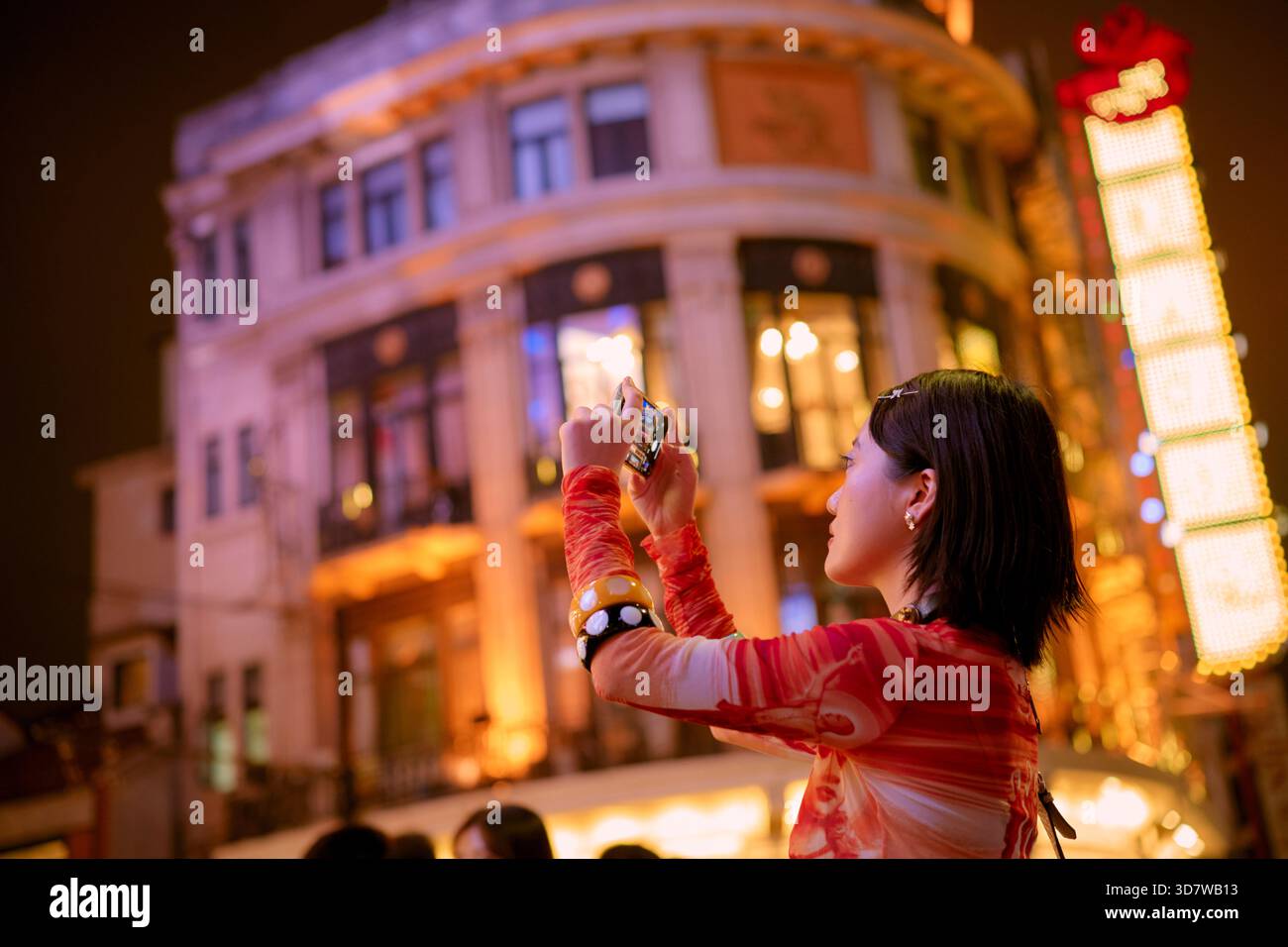 Woman in bright attire takes photo at night in a vibrant urban setting ...
