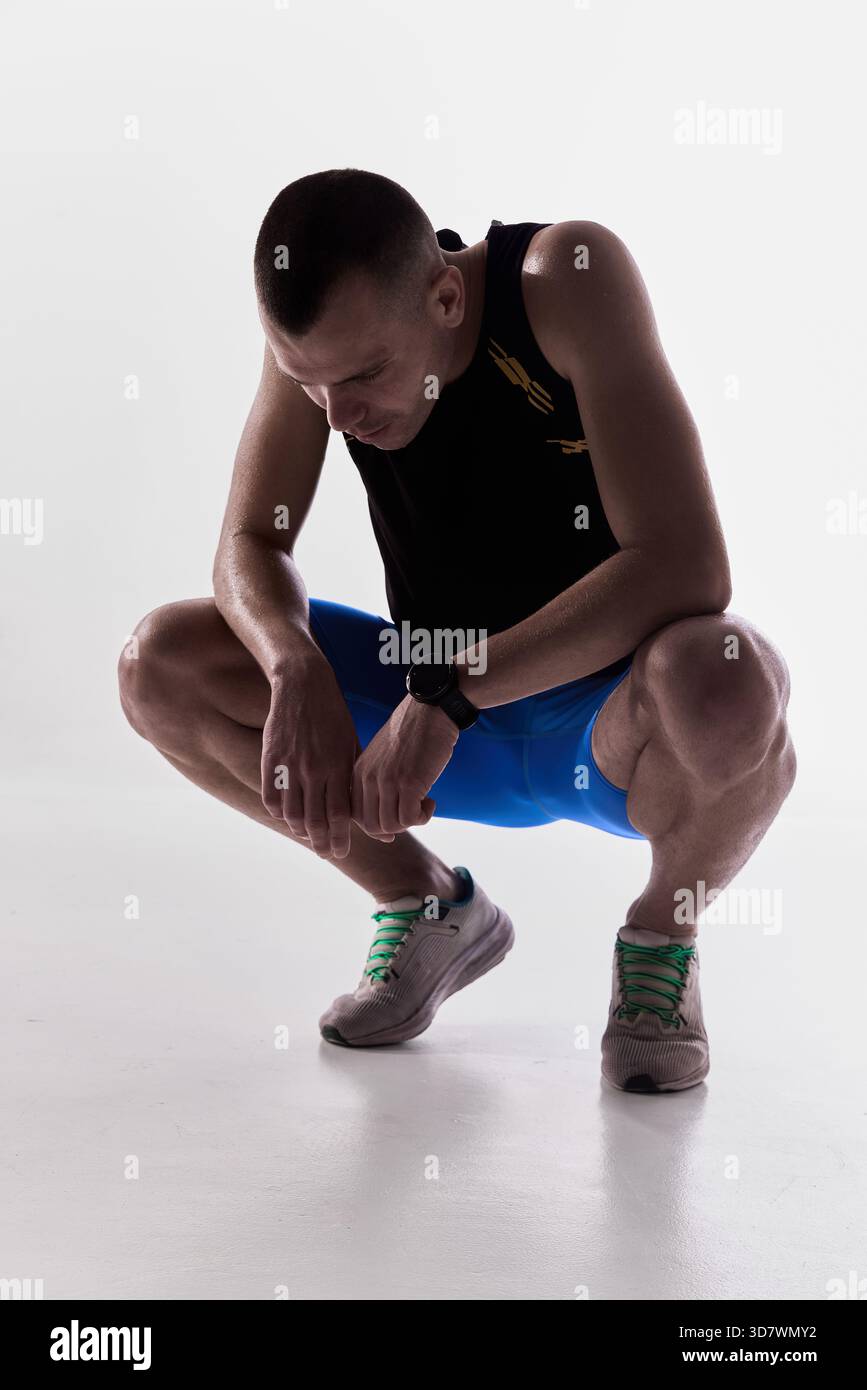 Runner squatting low after training to catch breath in white studio ...