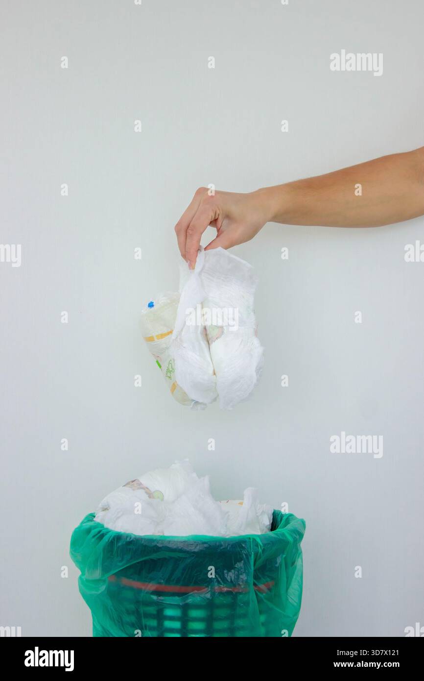 A woman's hand disposing of a used baby diaper into a trash can with a ...