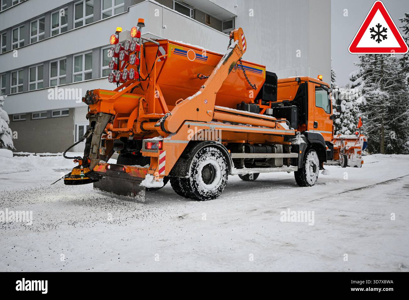 Orange gritter truck salting a snow covered road during freezing winter ...