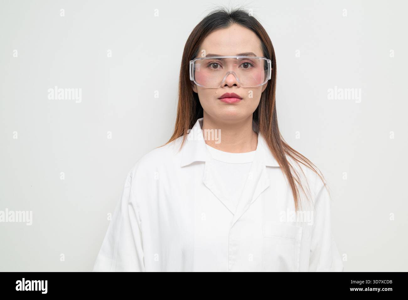 Studio portrait of an Asian scientist wearing a white lab coat and protective glasses. Serious ...
