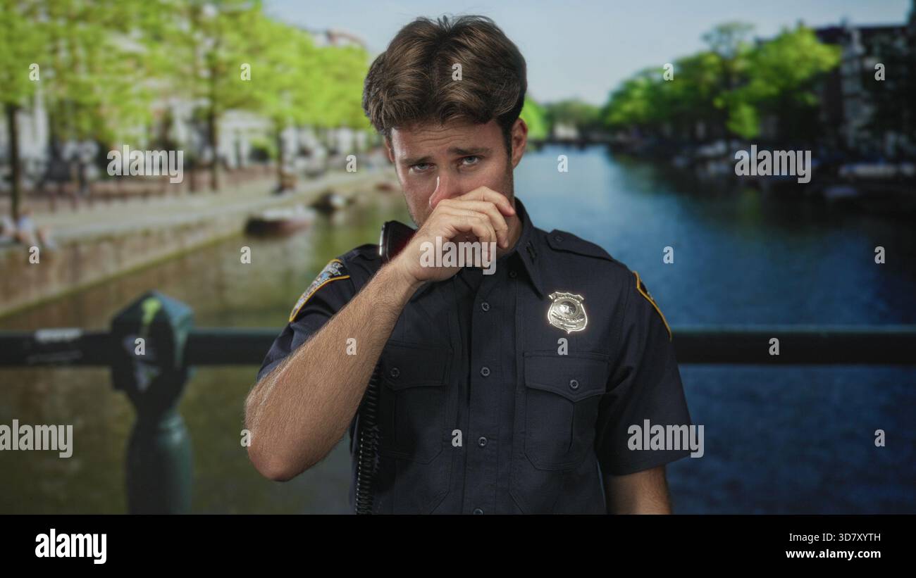 Man police officer pinches nose on street by a canal, badge visible and ...
