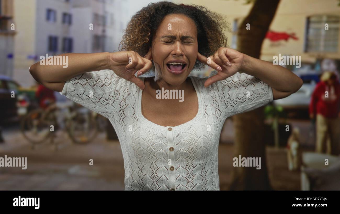 Woman pressing fingers into ears on street with bicycles and buildings ...