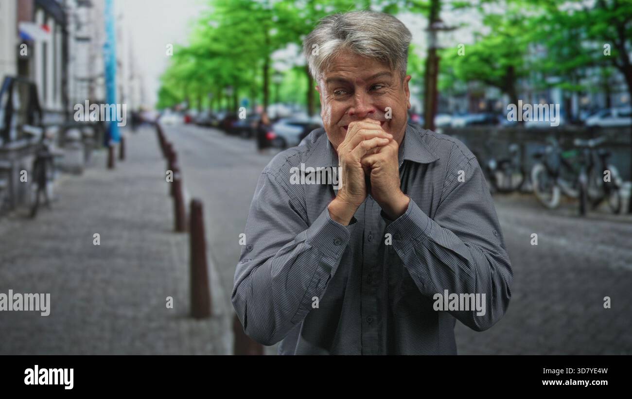 Man clasping hands to mouth on a street, biting knuckles with tense ...