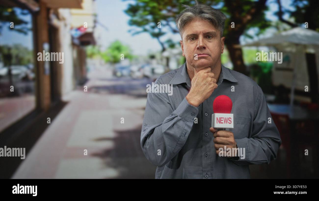 Man reporter holding red microphone, finger to temple during street ...