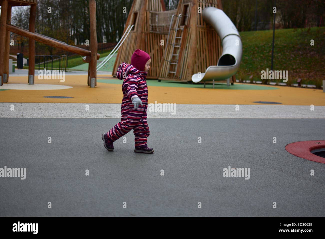 Toddler girl in a striped winter overall walking confidently across a ...