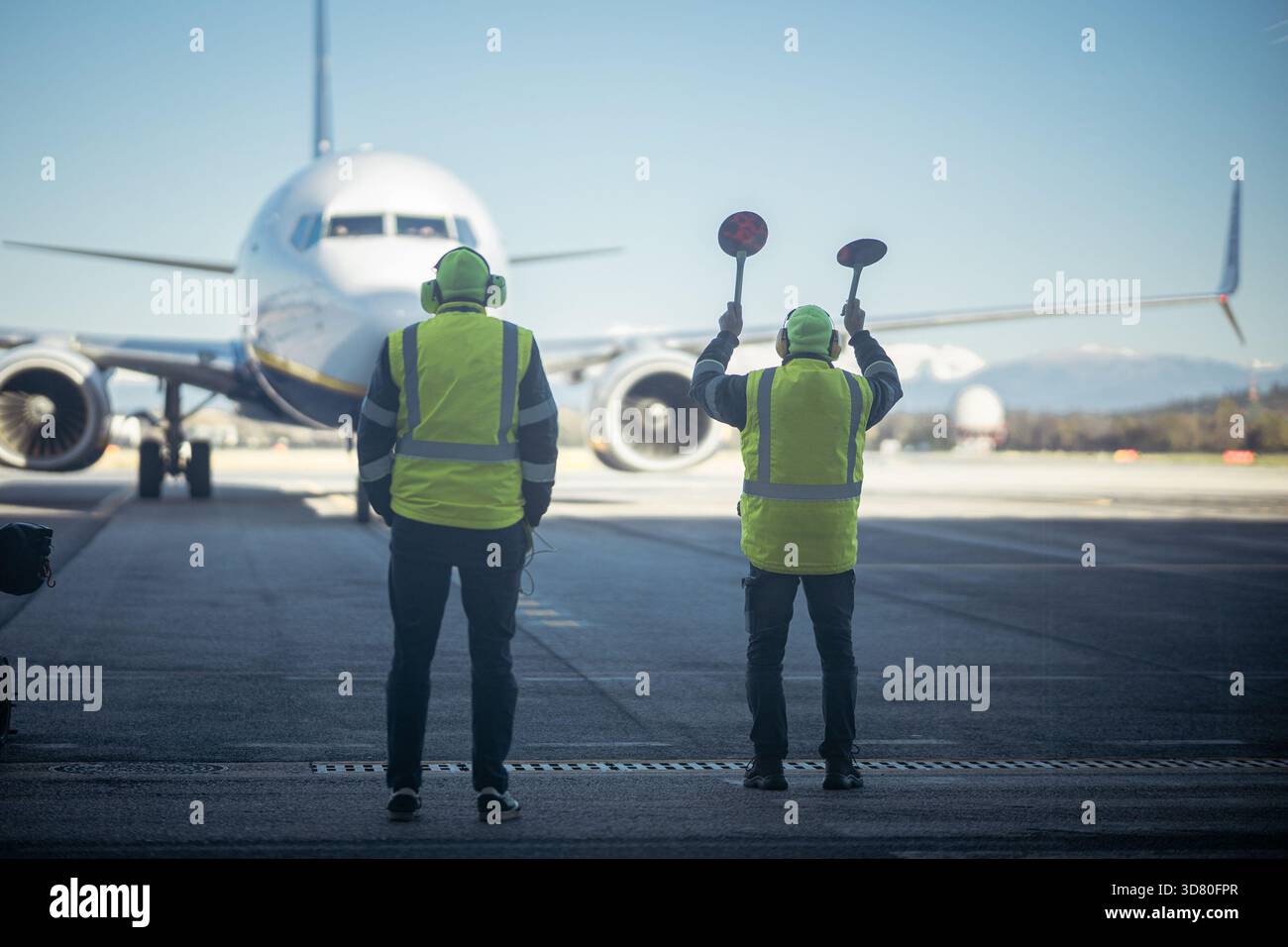 Two ground crew members in high-visibility gear guide an approaching ...
