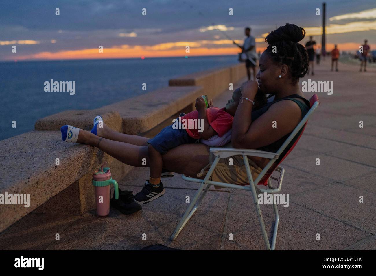A woman and a child lounge on the boardwalk during sunset in Montevideo ...