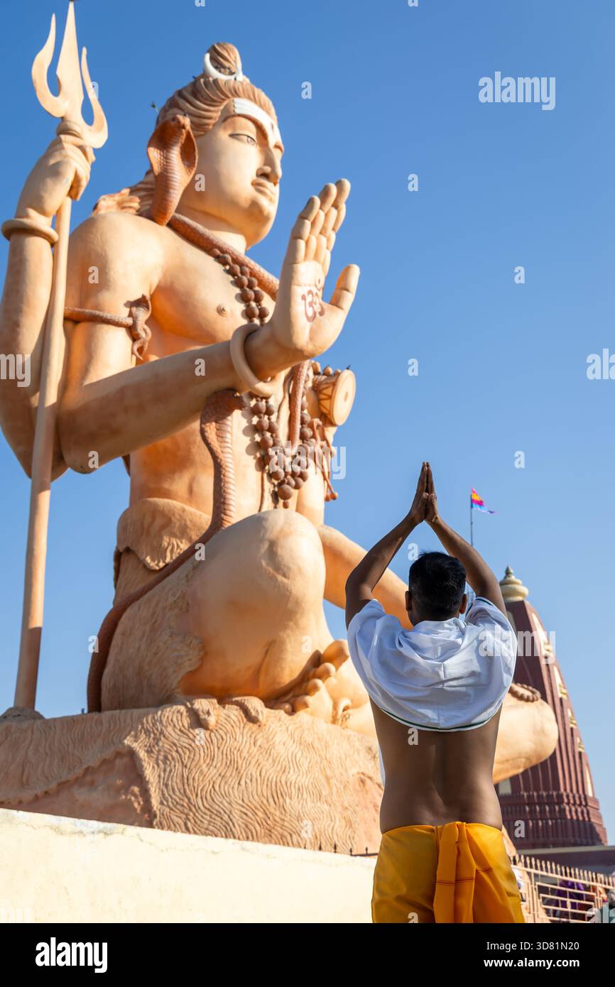 man performing reverent gesture toward giant deity figure framed by ...