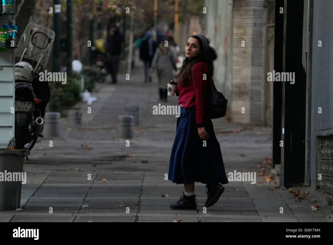A woman holds her drink as she walks on a sidewalk in northern Tehran ...