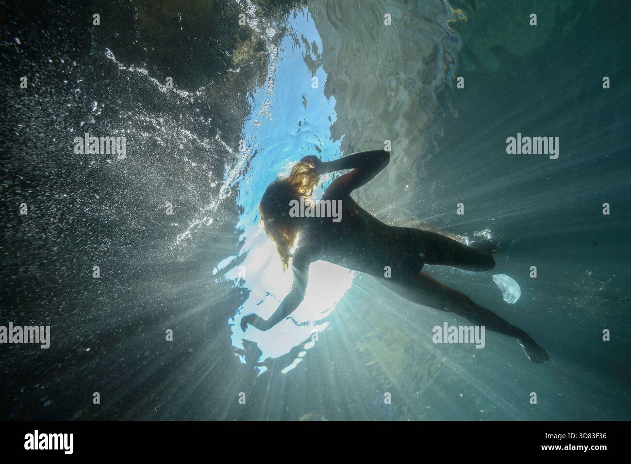 Underwater photo of a person swimming in sunlight rays through clear ...
