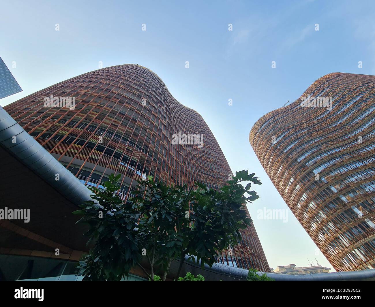 Curved twin towers with orange facade rising behind urban greenery ...