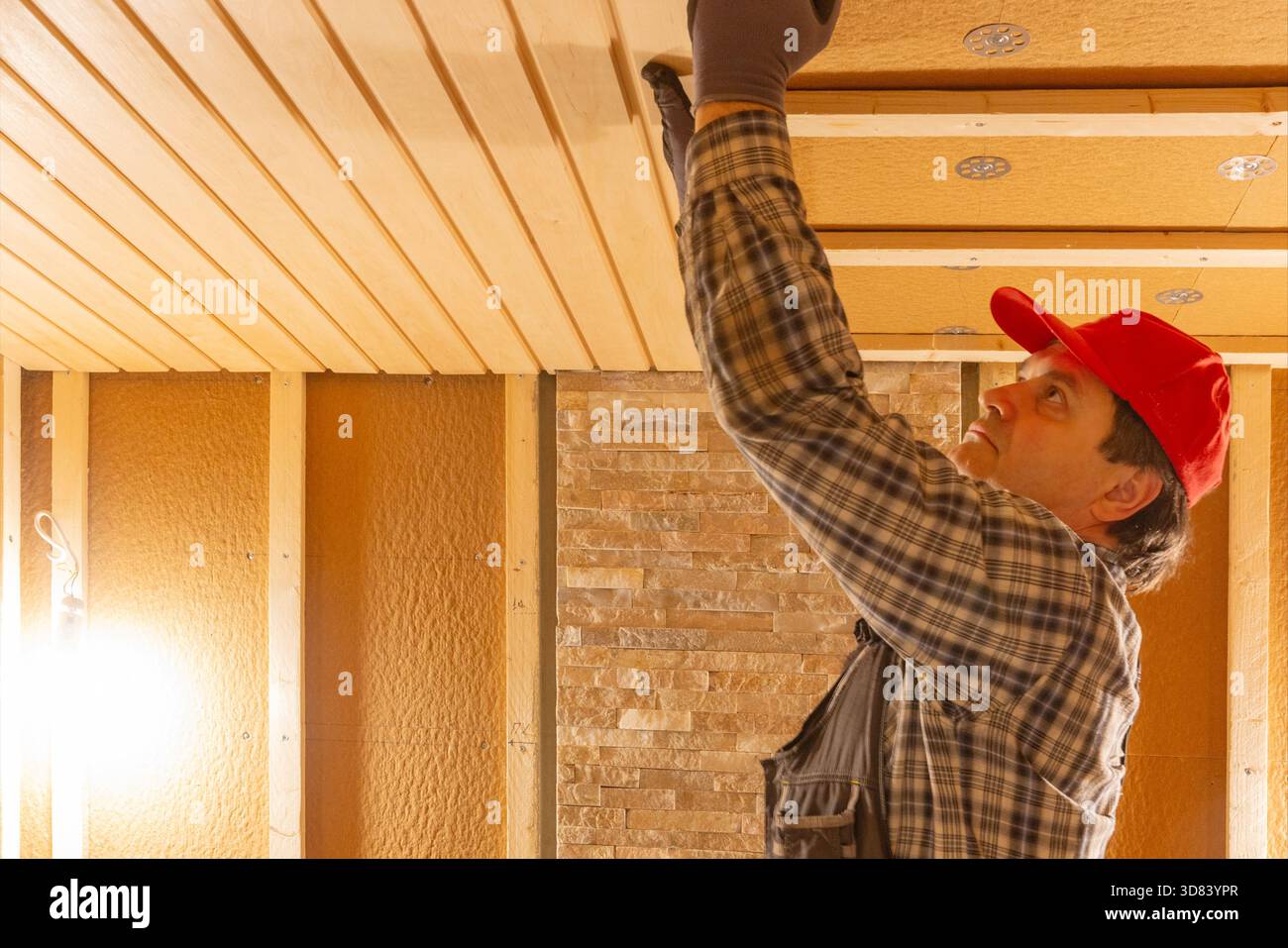 Worker lifting wooden ceiling board inside unfinished room, insulation ...