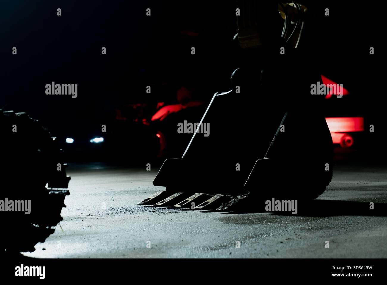 Heavy machinery bucket touching the worksite floor in low-light ...
