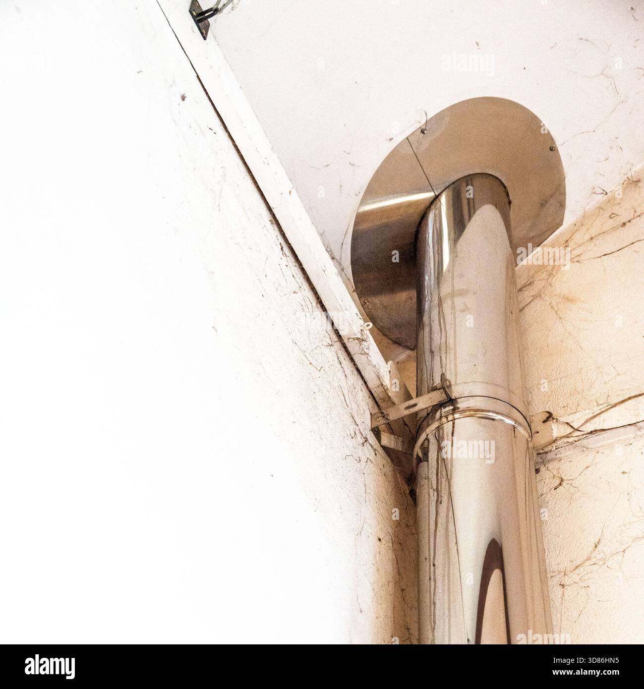 A stainless steel chimney pipe is installed against a white wall ...