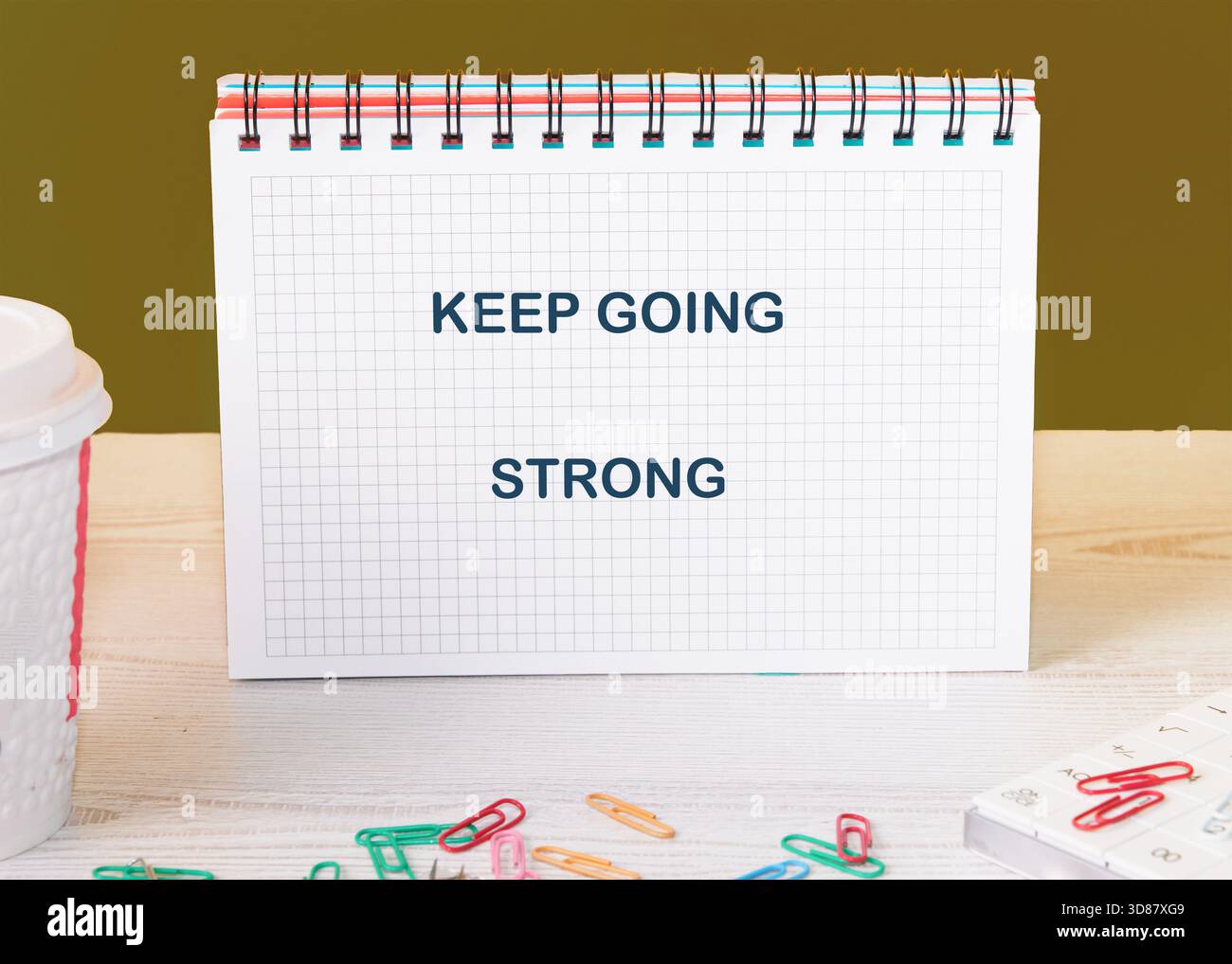 A notepad with a motivational message sits on a desk scattered with ...