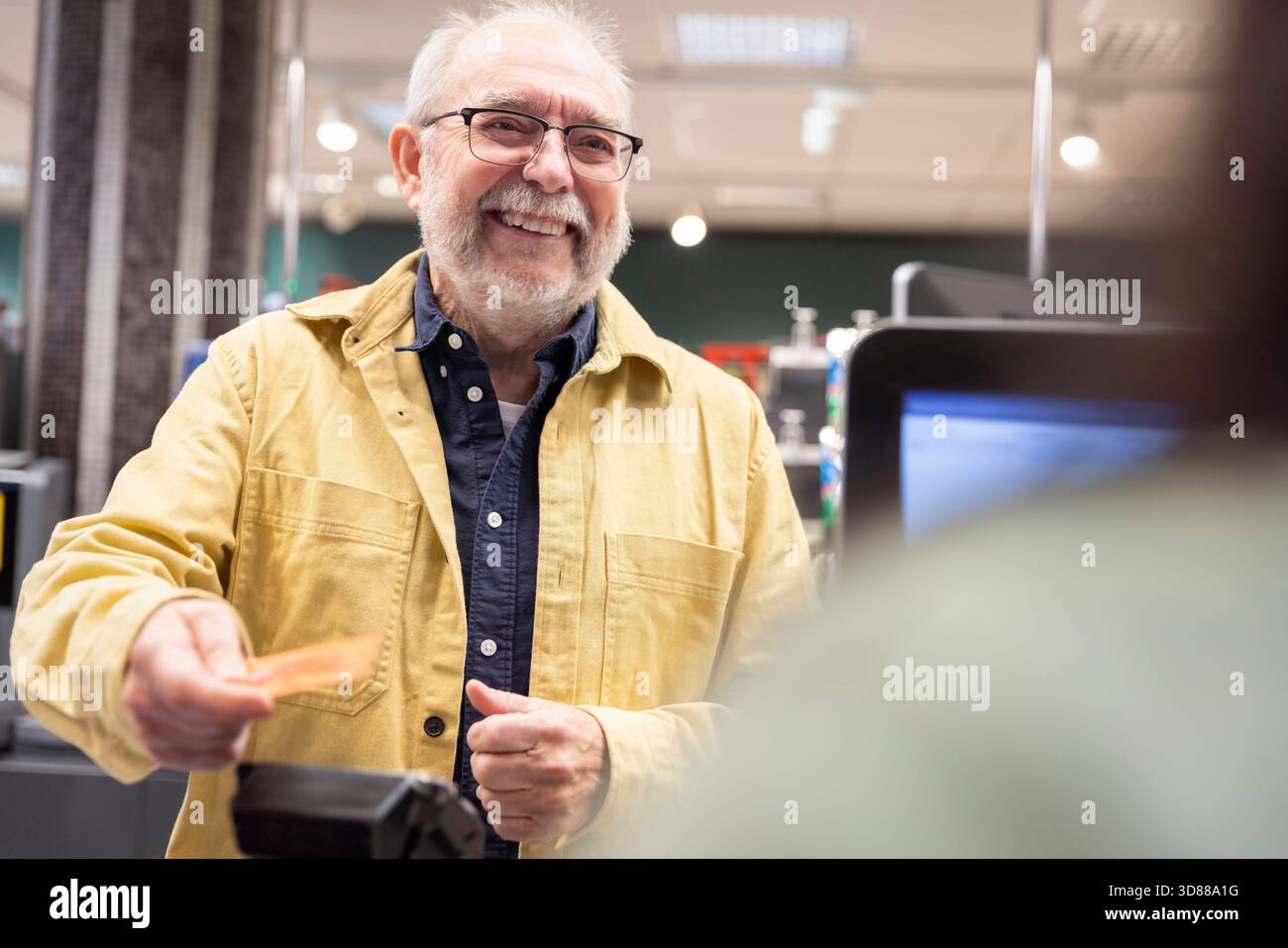 Smiling senior man giving credit card to cashier at supermarket ...