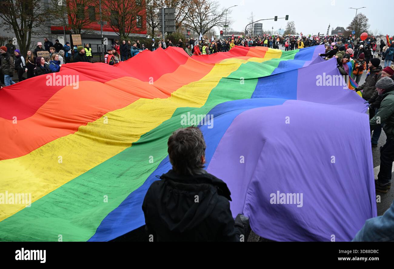 29 November 2025, Hesse, Gießen: Demonstrators wave a rainbow flag. The ...